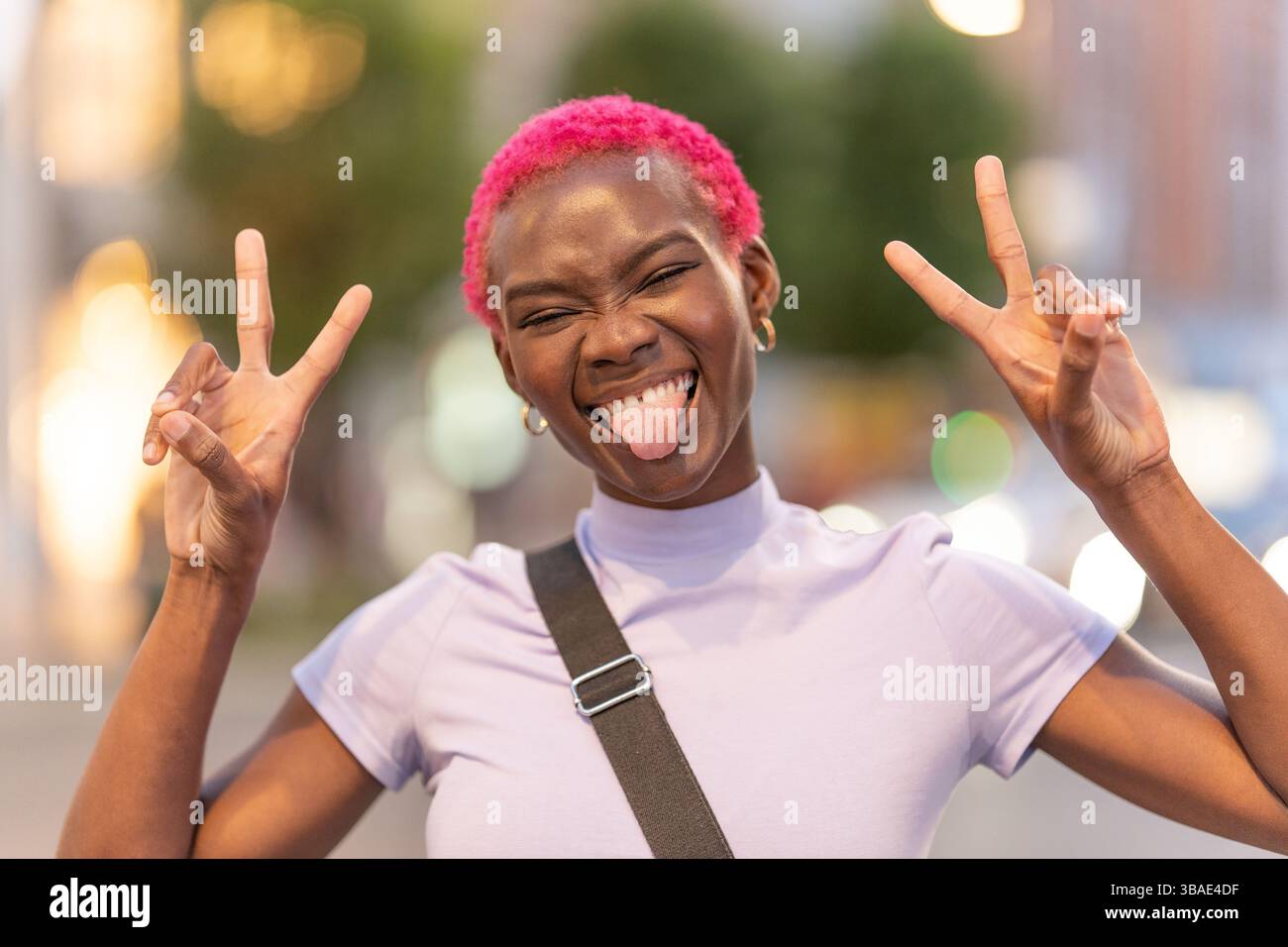 Black female with short dyed hair making face doing peace hand sign ...