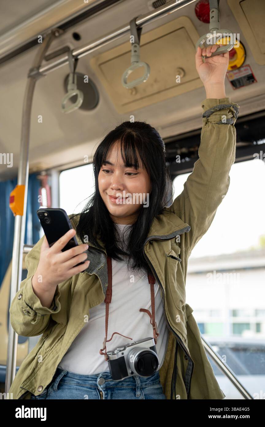 A positive Asian female solo traveler using her smartphone while ...