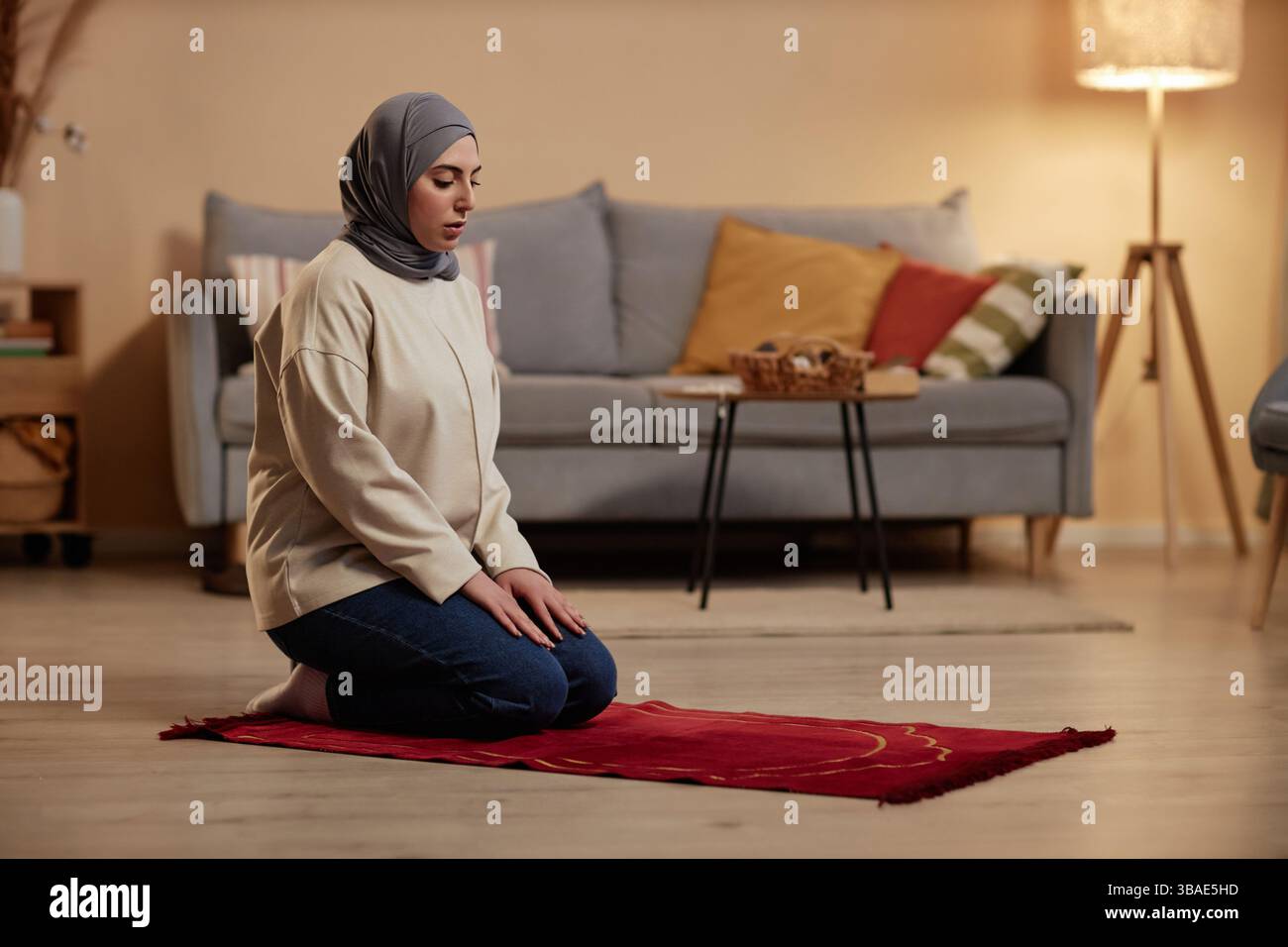 Mixed-race Muslim woman in hijab keeping her eyes closed while kneeling ...