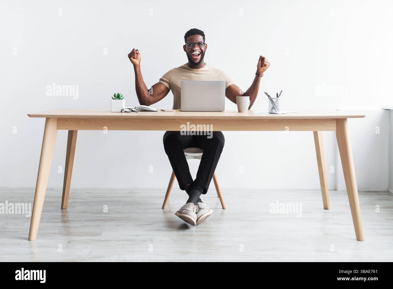 Excited young black office employee sitting at desk with laptop ...