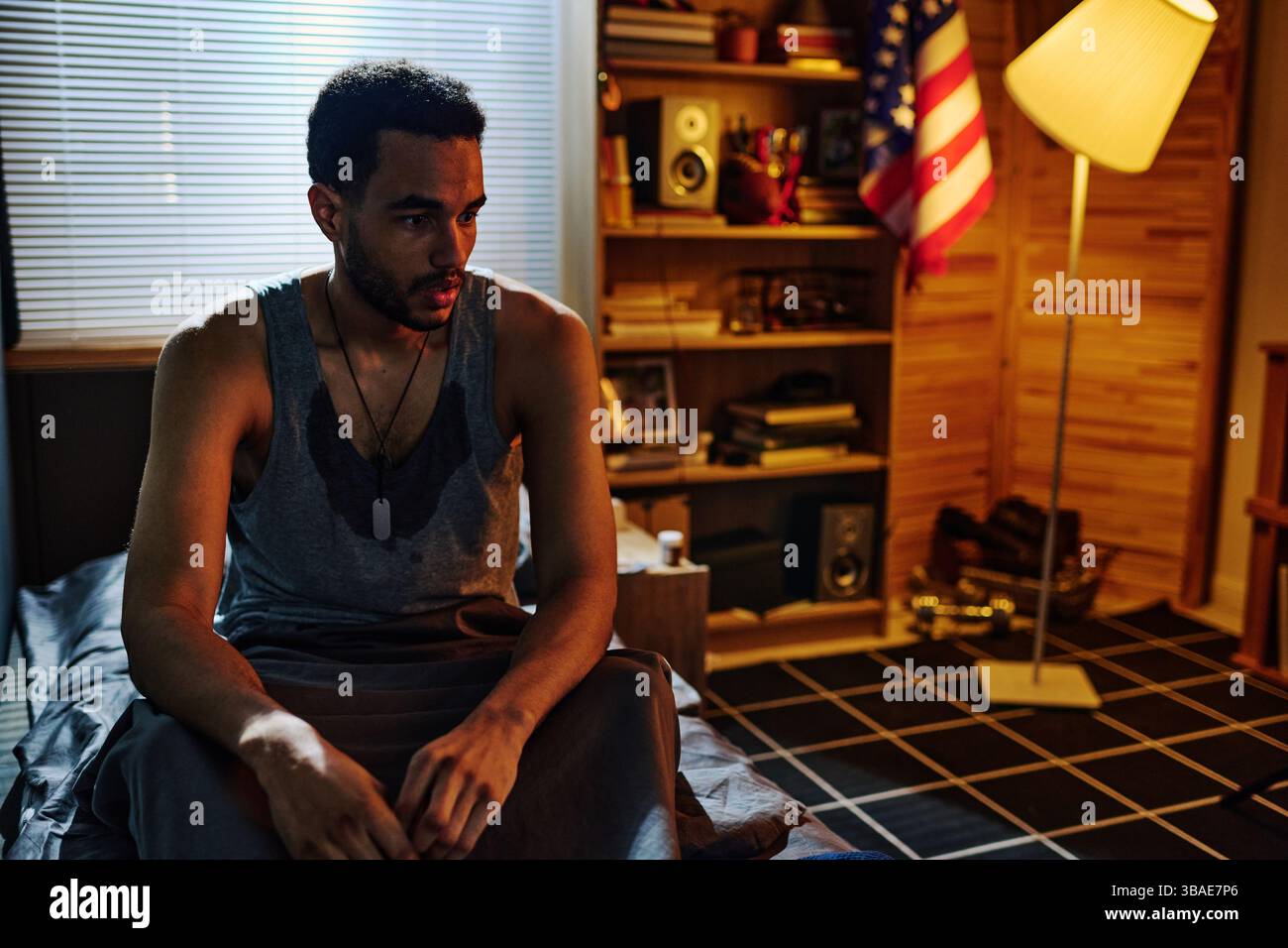 Young sweaty man in grey wet vest sitting on bed in the middle of the ...