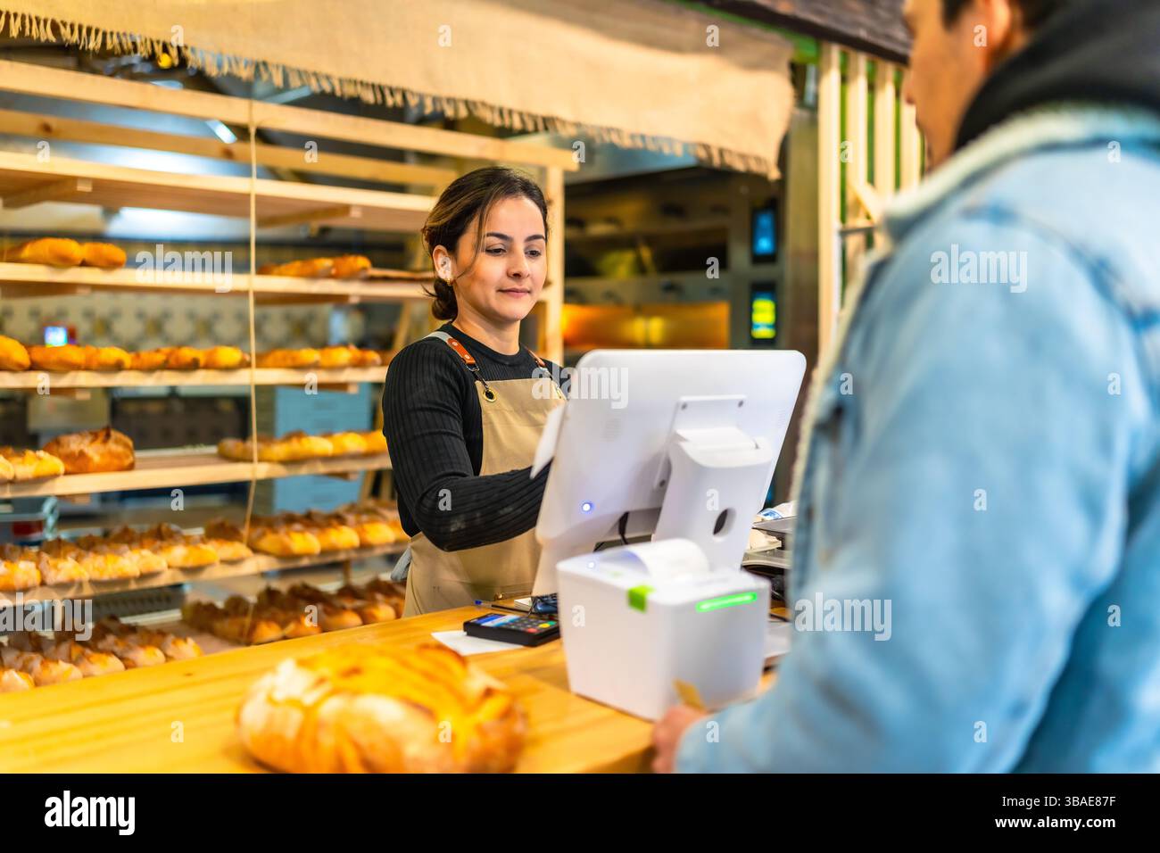 Hispanic female baker in apron using touchscreen computer to calculate ...