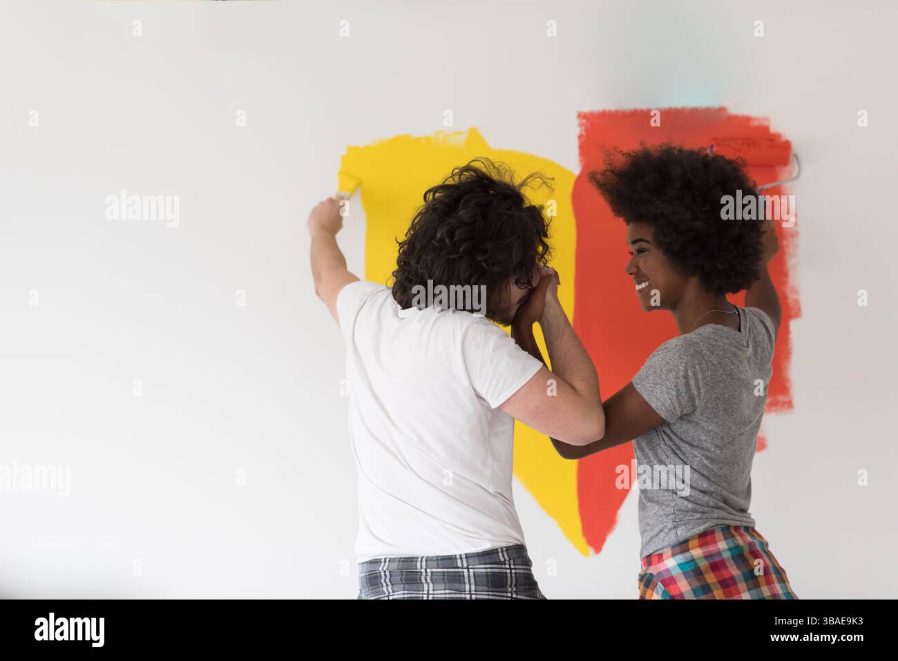 Black and caucasian couple cuddling and kissing while painting wall of ...
