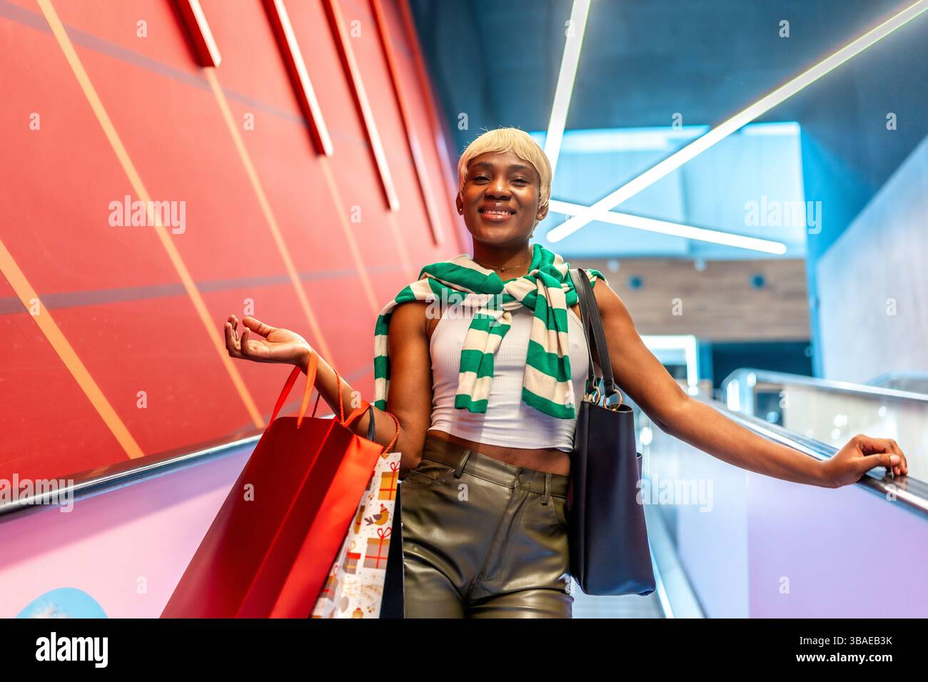 Urban african woman standing on escalator carrying shopping bags and smiling at camera Stock ...