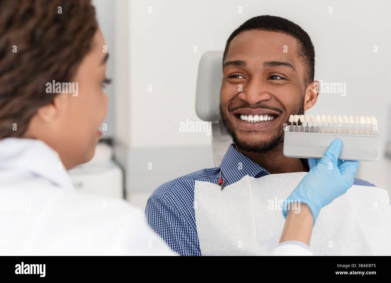 Cheerful african patient and female dentist choosing filling shade ...