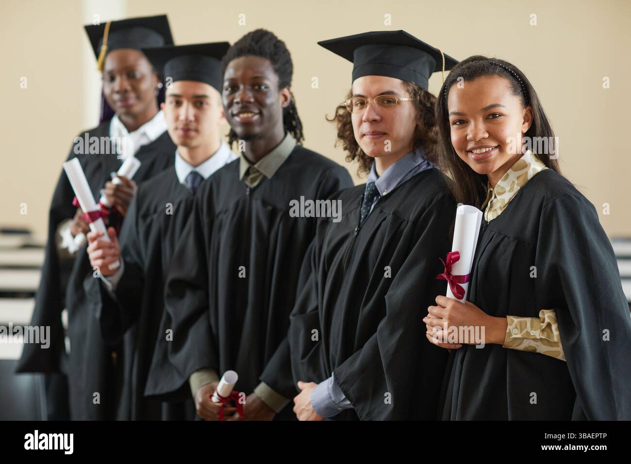 Diverse group of students wearing graduation gowns holding their ...