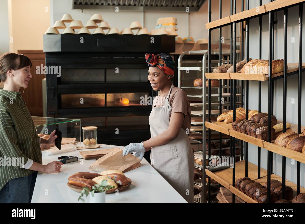 African young woman packing fresh bread and selling it to the customer ...