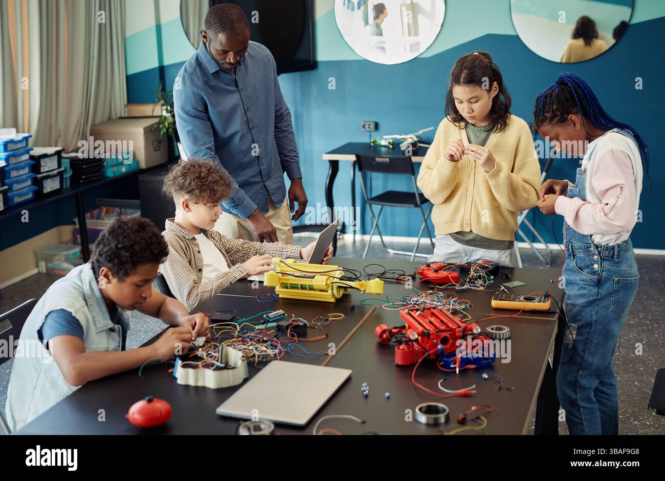 Diverse group of teenage children building robots together while enjoying engineering class in ...
