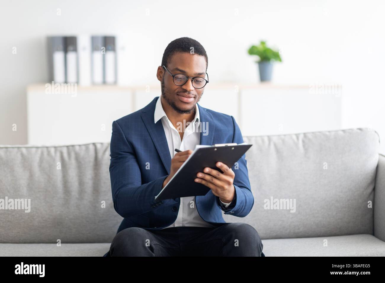 Focused black male psychologist sitting on couch and writing in ...