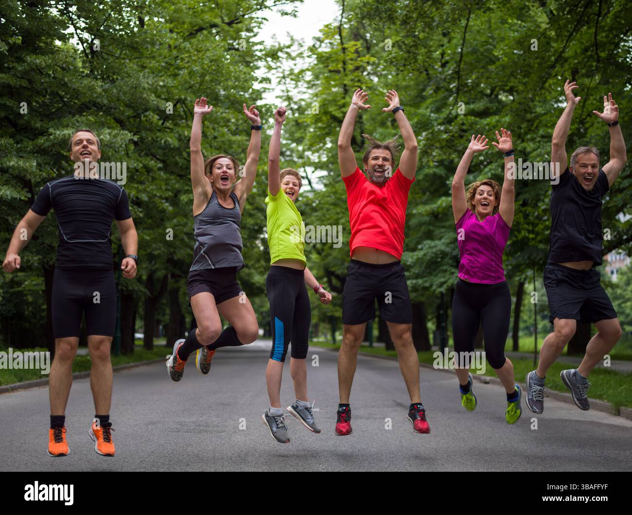 group of healthy runners team jumping in the air at city park during ...