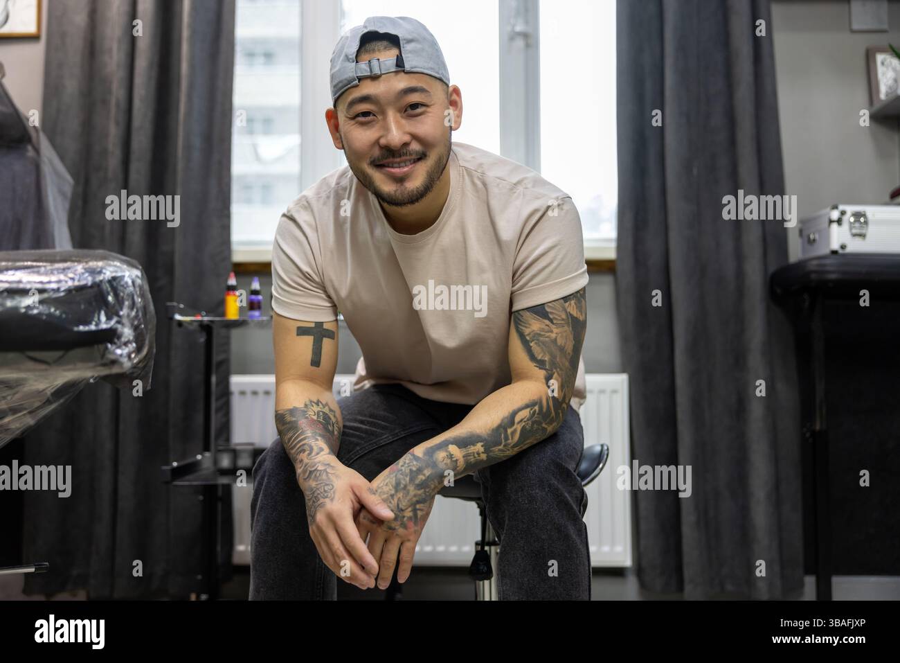 Smiling Asian male tattoo artist leaning forward sitting in his tattoo ...
