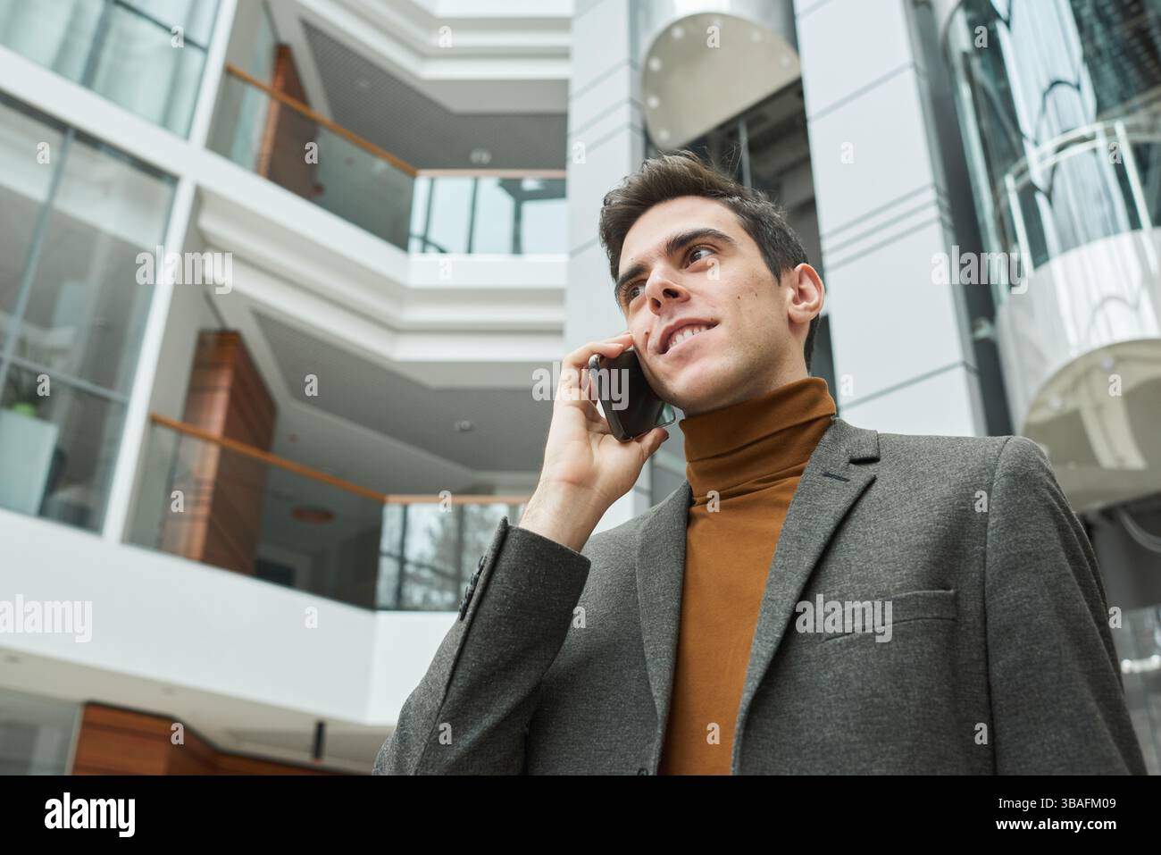 Mixed-race businessman having phone call and looking away standing inside the office building ...