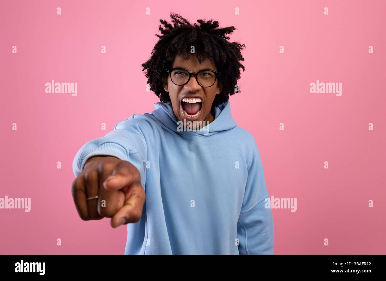 Angry black teenager shouting and pointing at camera on pink studio ...