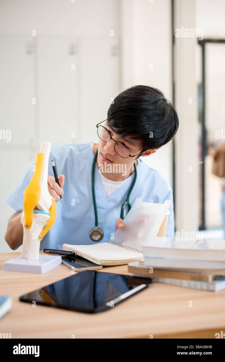 A smart Asian male medical student in scrubs is examining a model of ...