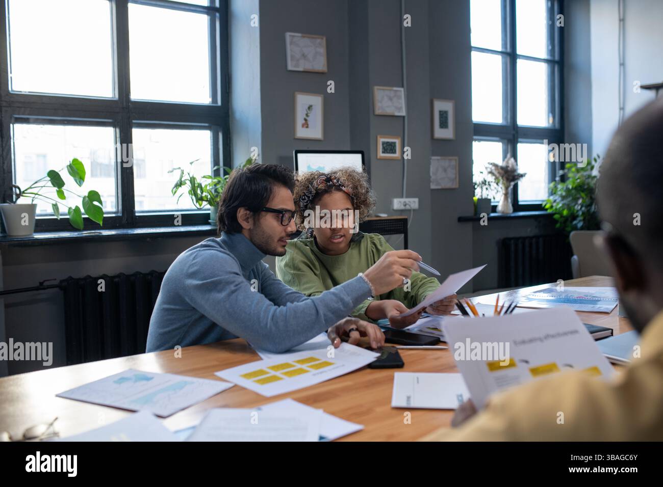 Young man pointing at paper while explaining data to biracial colleague ...