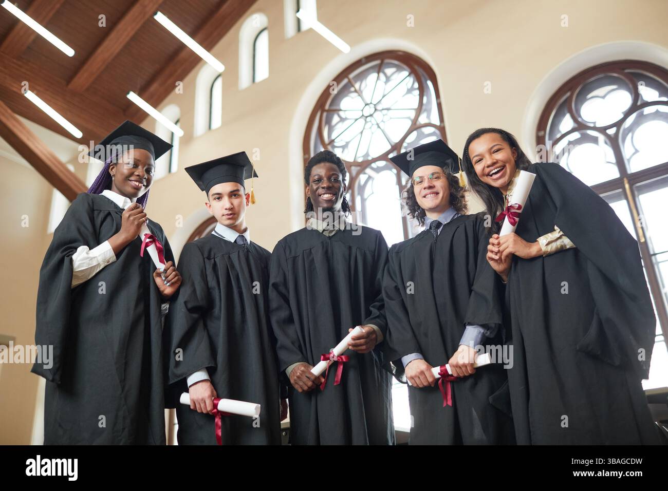 Diverse group of students wearing graduation gowns holding their ...