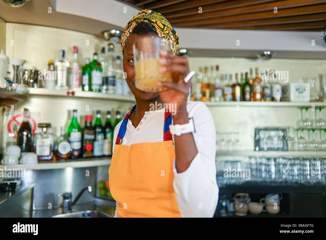 Black female bartender wearing headwrap and apron offering glass of ...