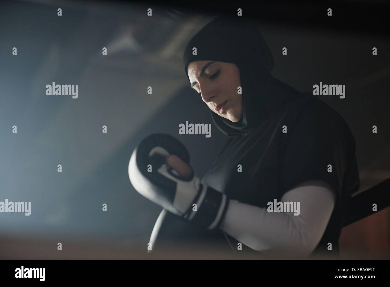 Mixed-race Muslim female boxer in hijab putting on boxing gloves before ...
