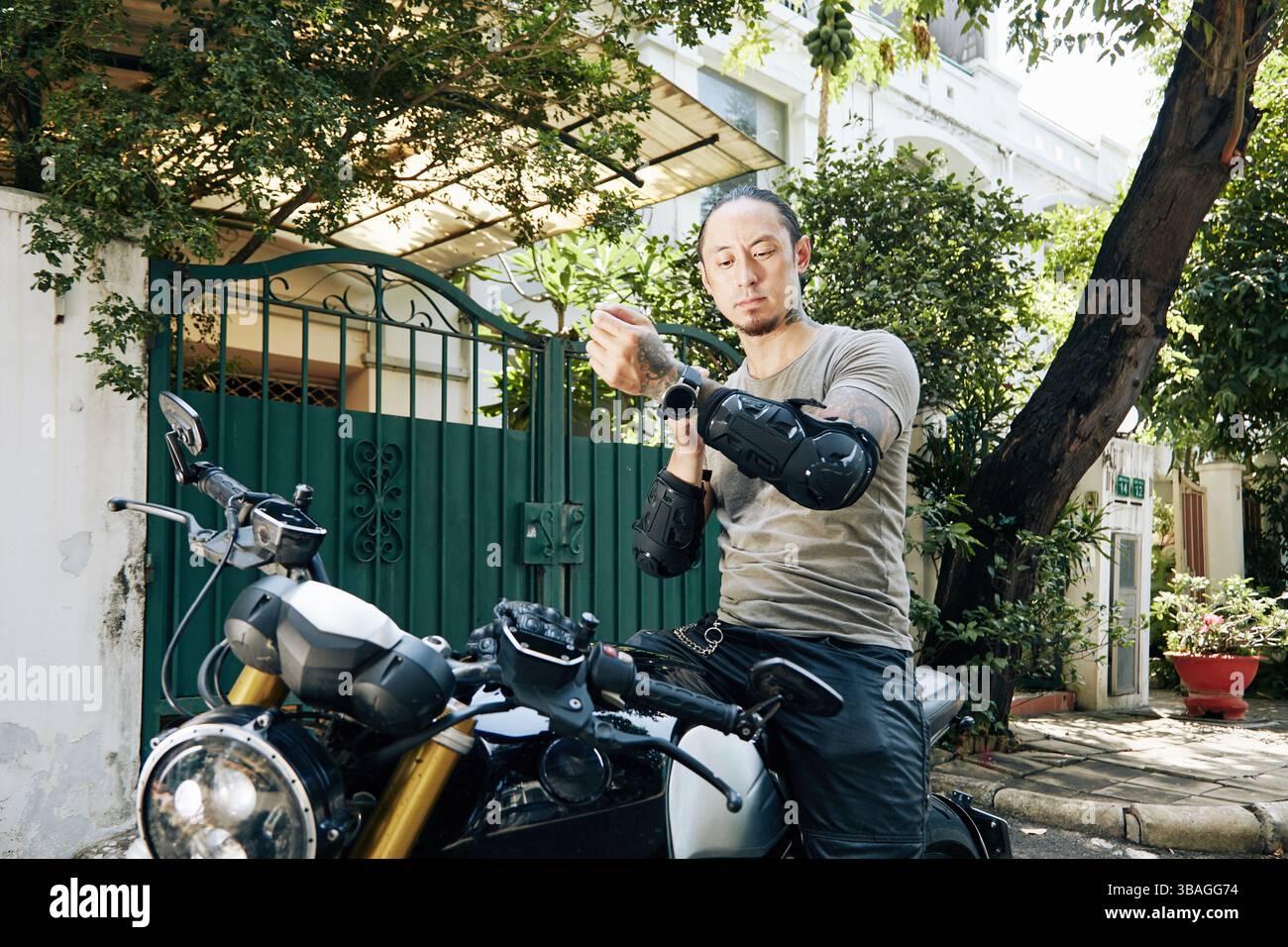 Frowning motorcyclist putting on forearm guard pads for protection when ...