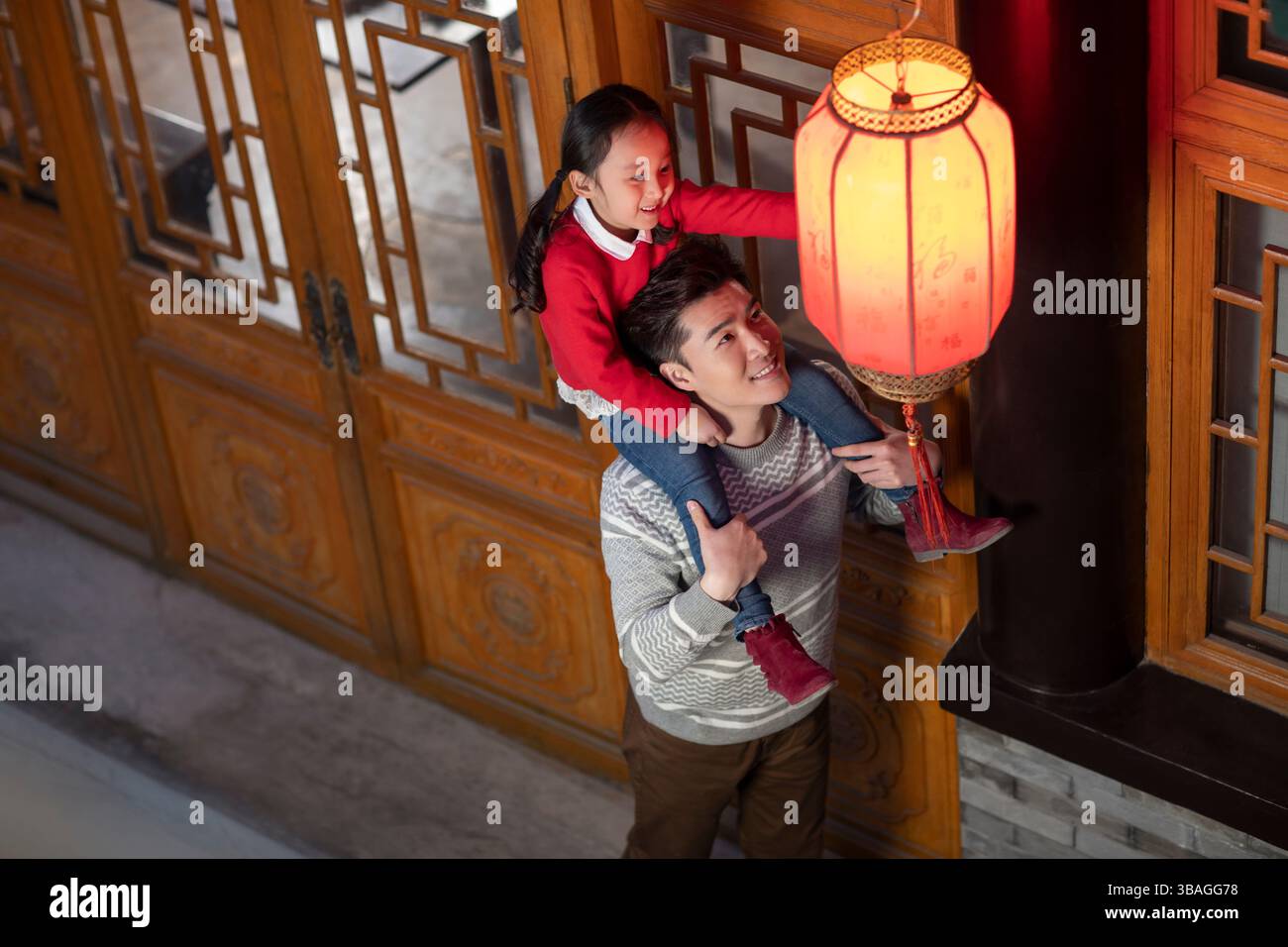 Smiling Chinese father carrying daughter on his shoulders while ...