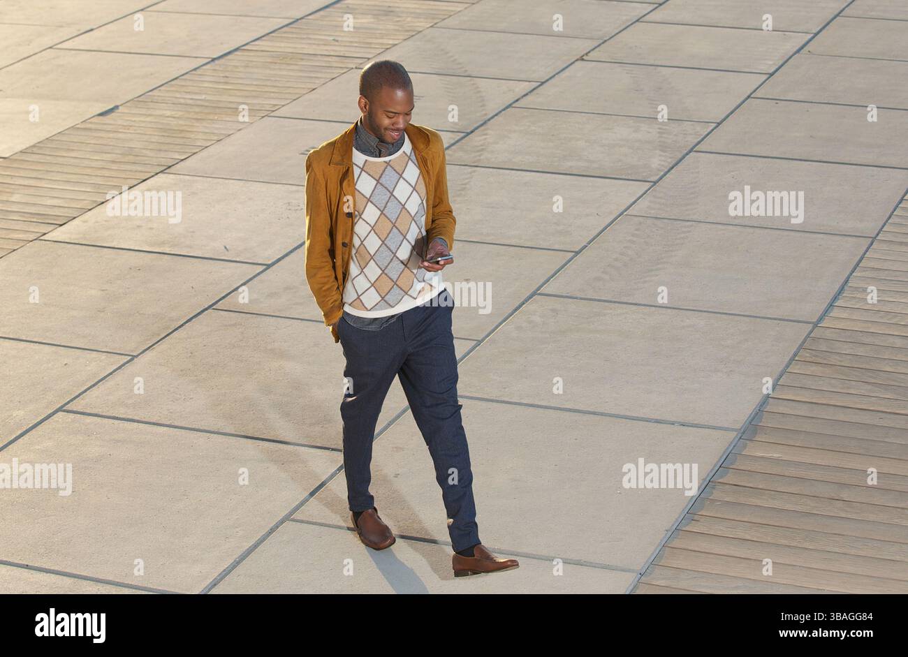 Portrait of a happy young man walking and sending message on mobile ...