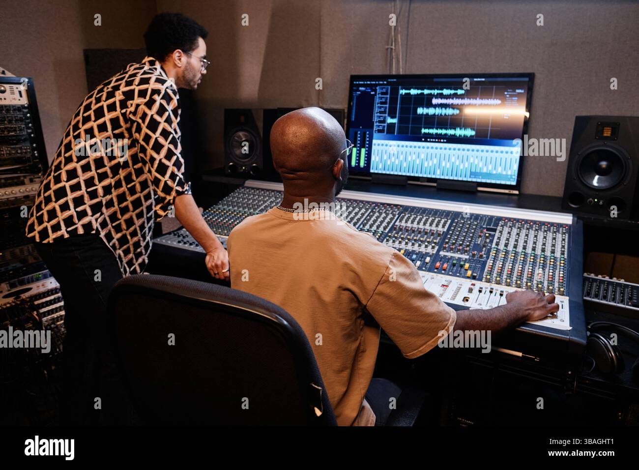 Black producer and singer creating music track using mixing console in ...