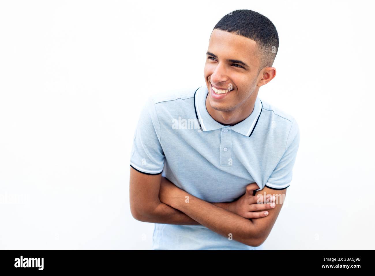 Smiling Arab male with crossed arms leaning forward against white wall ...