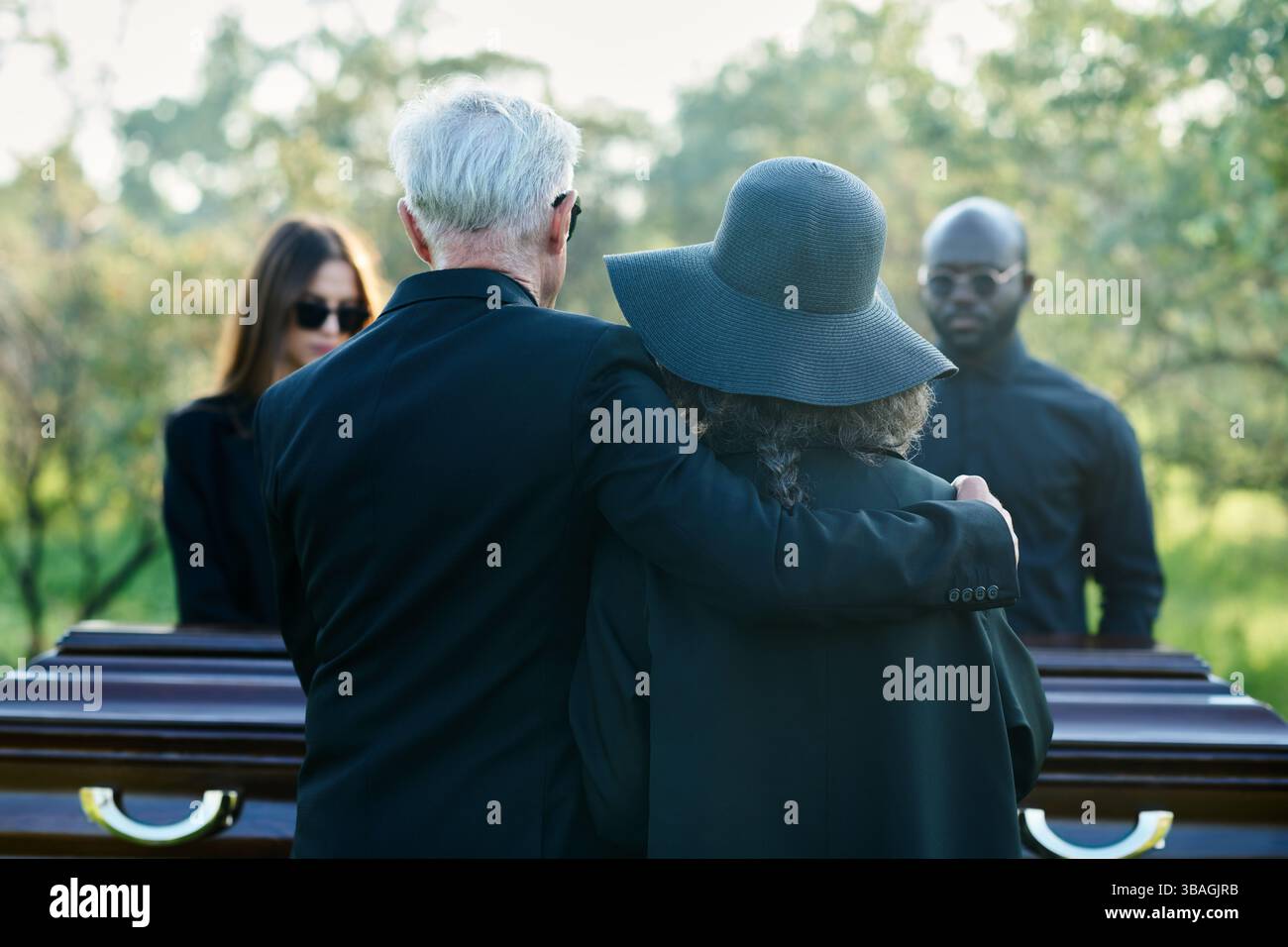 Rear view of mature grey haired man embracing his wife in black hat ...
