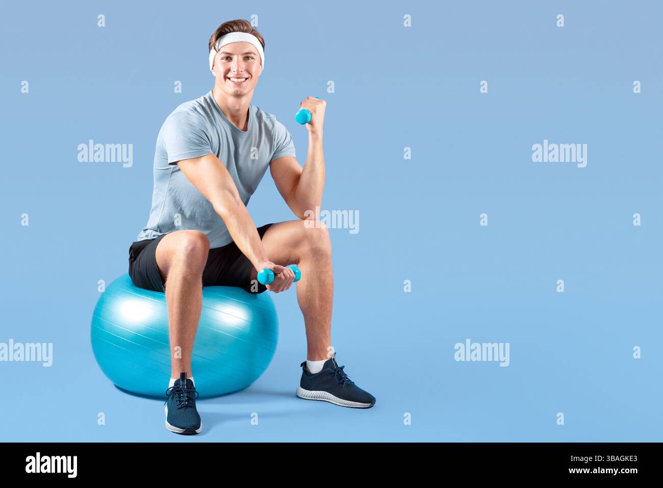 Happy millennial guy in sports clothes sitting on fitball and working ...