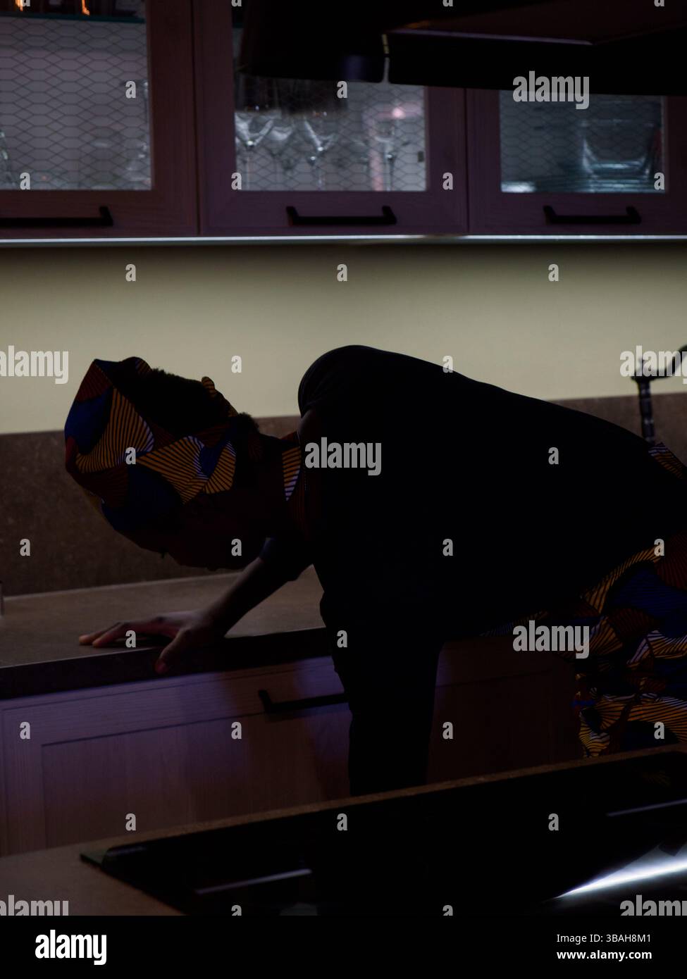 Black woman wearing bandana and apron bending over at kitchen counter ...