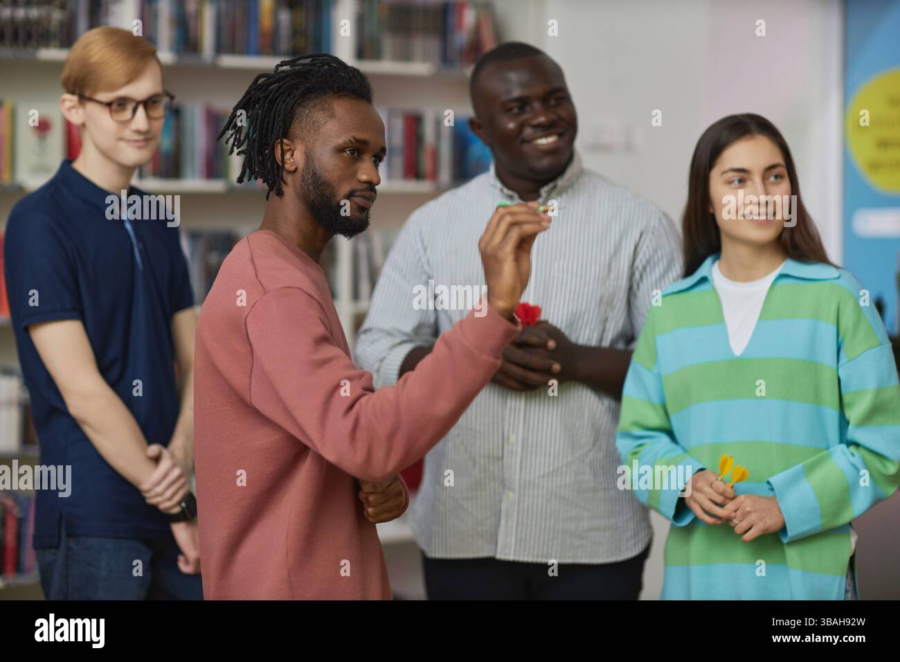 Portrait of black man playing darts game indoors with diverse group of ...