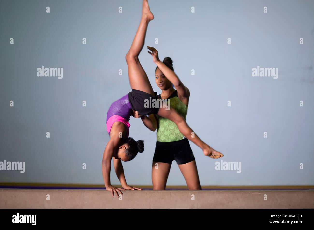 Hispanic female gymnast supporting younger gymnast performing back ...
