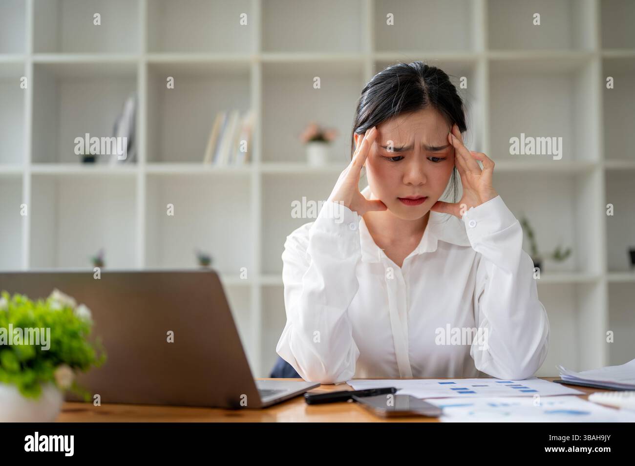 A stressed and frustrated Asian businesswoman sits at her office desk ...