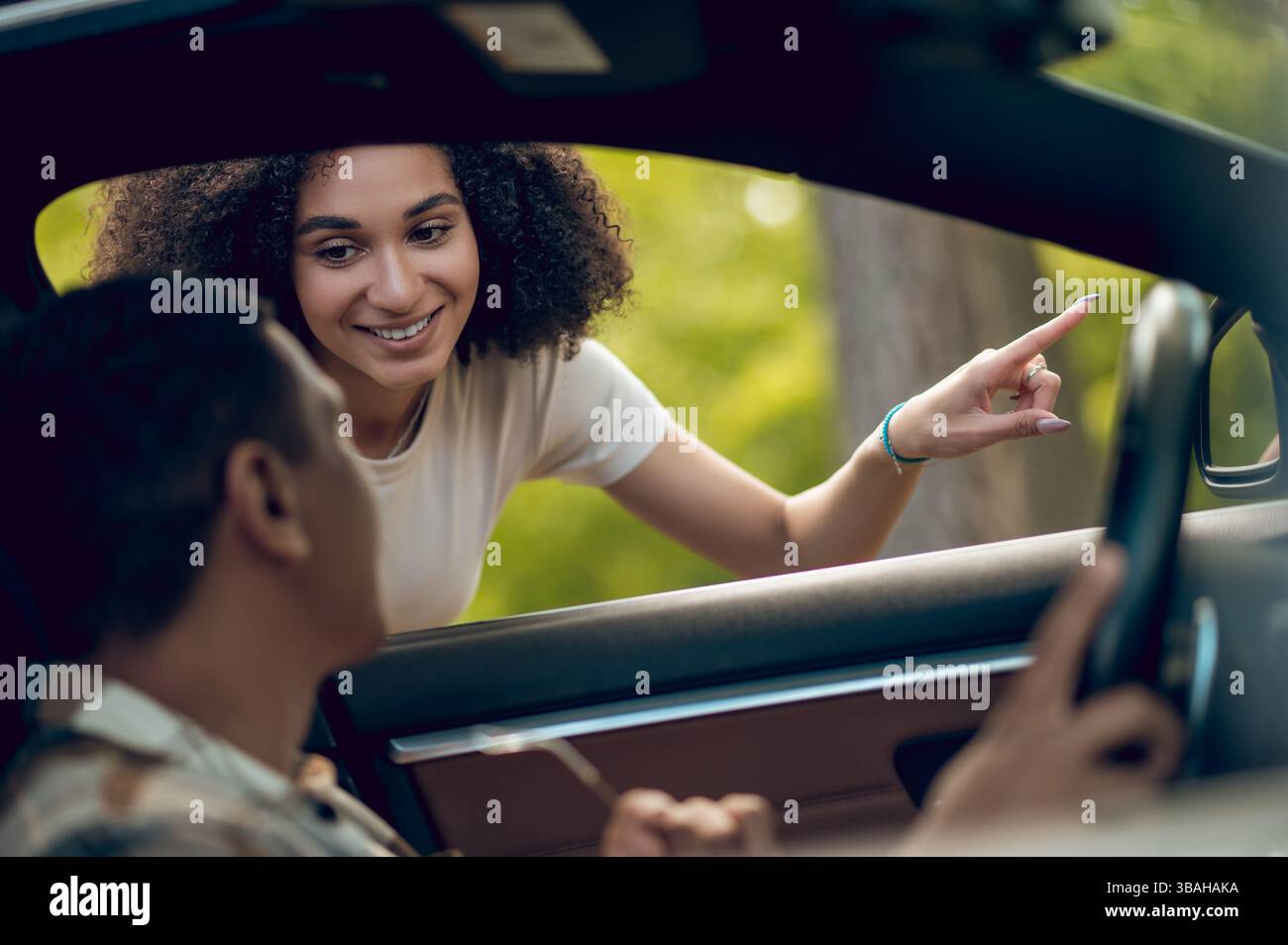 Smiling Black woman leaning forward and pointing finger away while ...