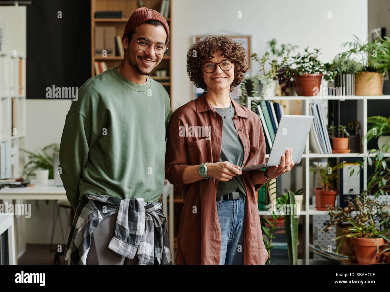 Two happy young intercultural programmers in casualwear looking at you with smiles while one of ...