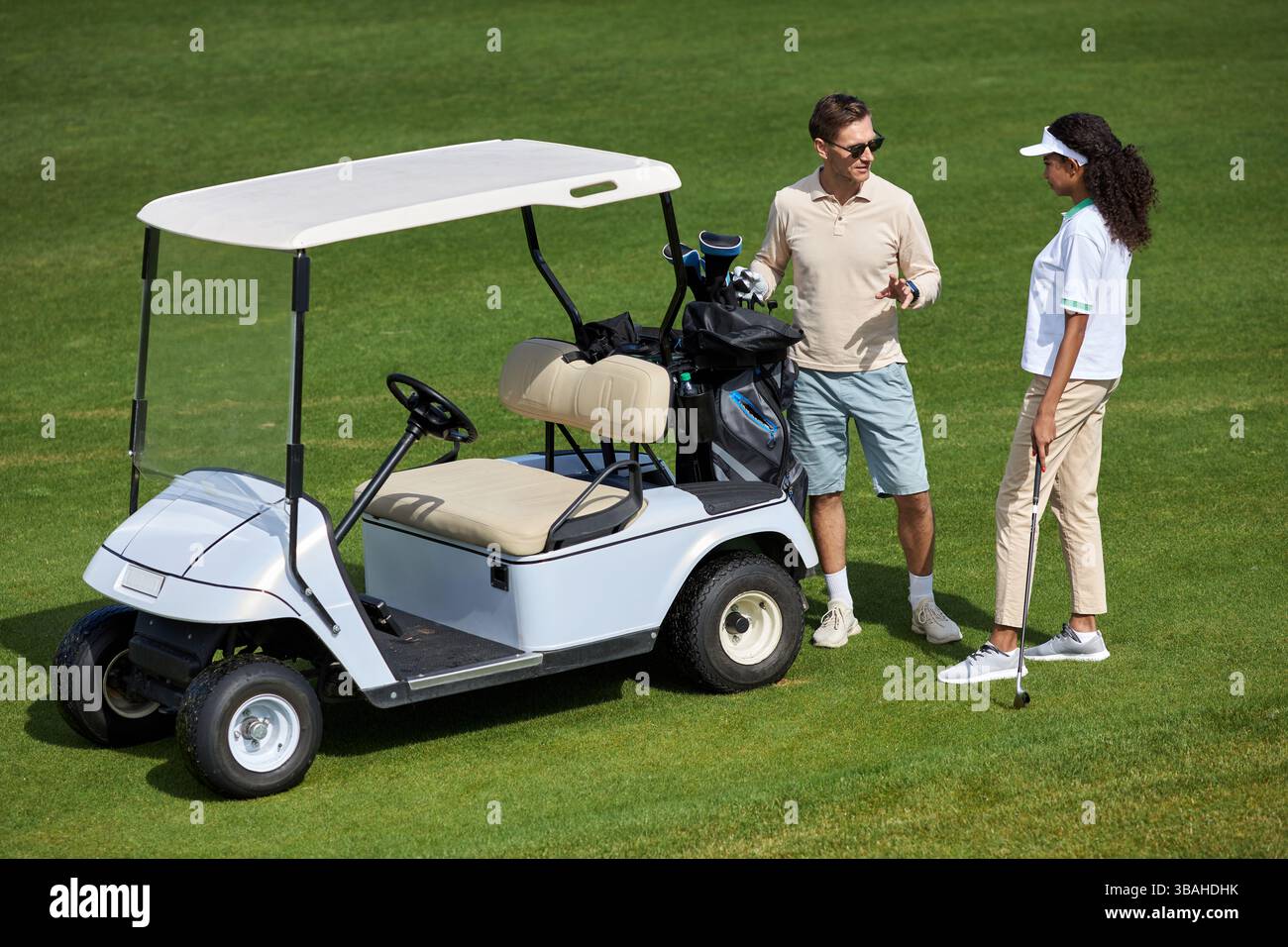 Mixed-race female golfer wearing vizor cap talking to her caucasian ...