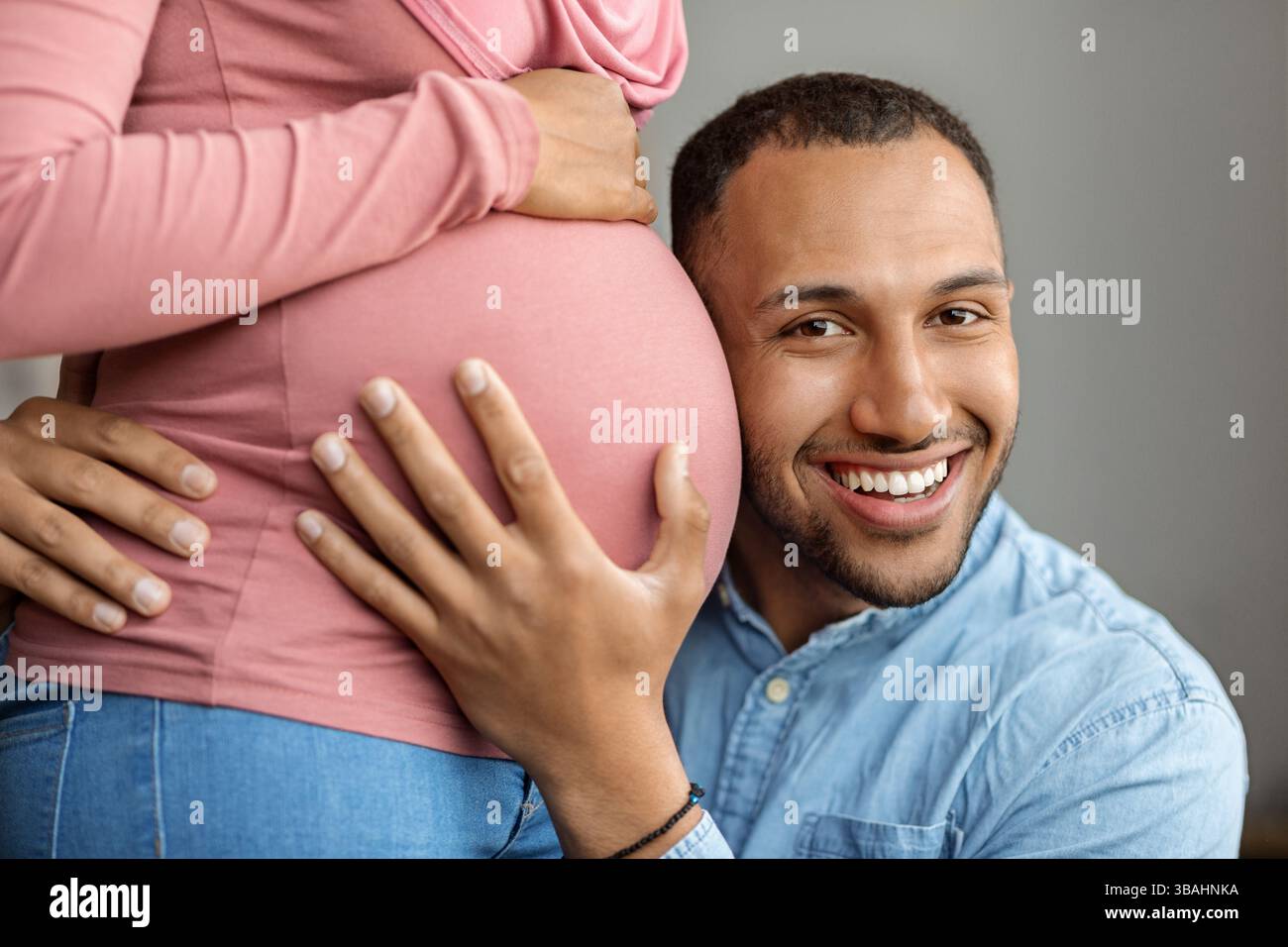 Happy Black man embracing belly of his pregnant Muslim wife listening ...