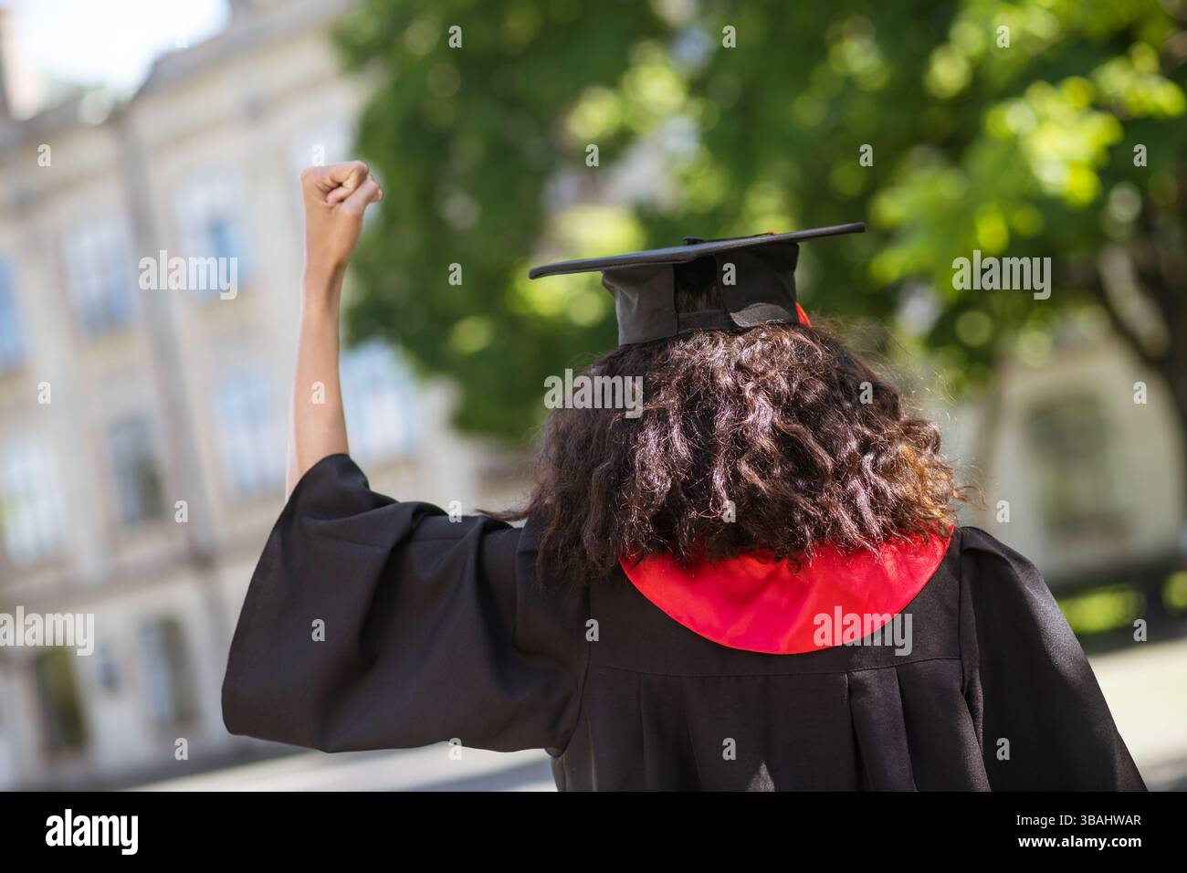 African American female in graduation gown raising closed fist standing ...