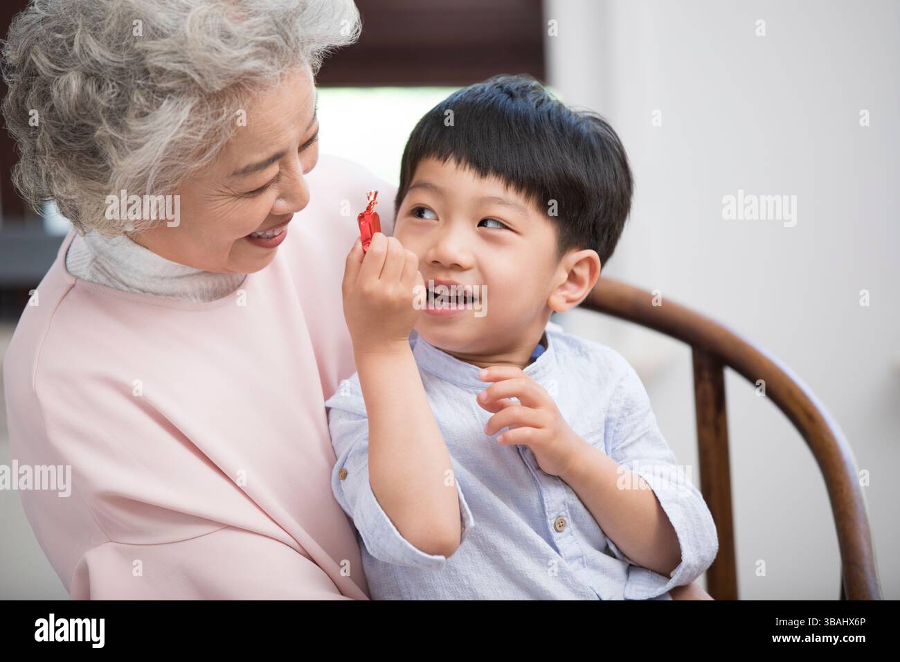 Smiling Chinese boy holding candy while sitting on lap of his ...