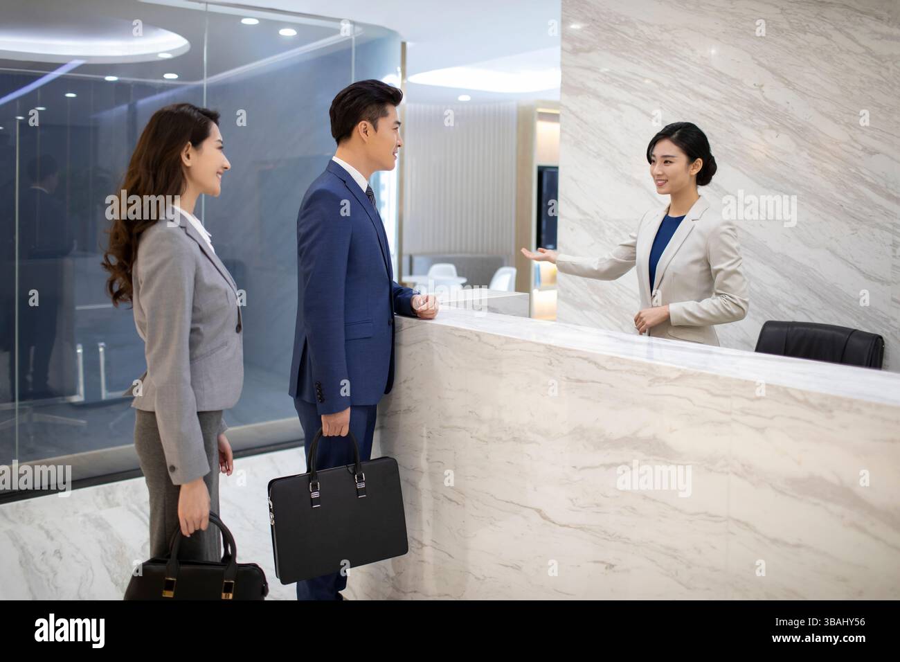Smiling Chinese business people talking to female receptionist while ...
