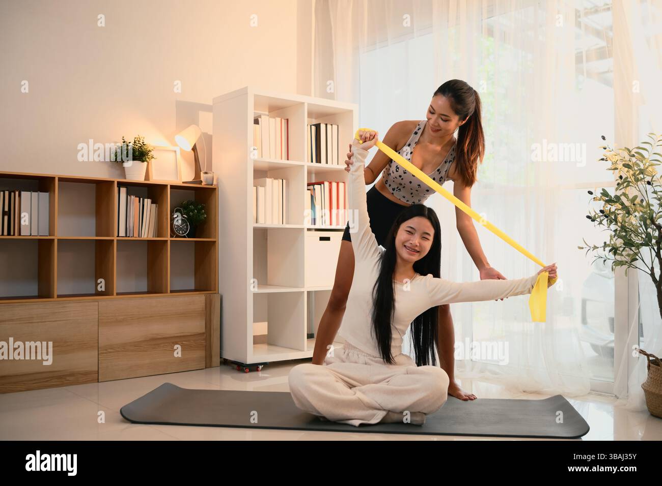 Mother helps daughter stretch with resistance band during fun home ...