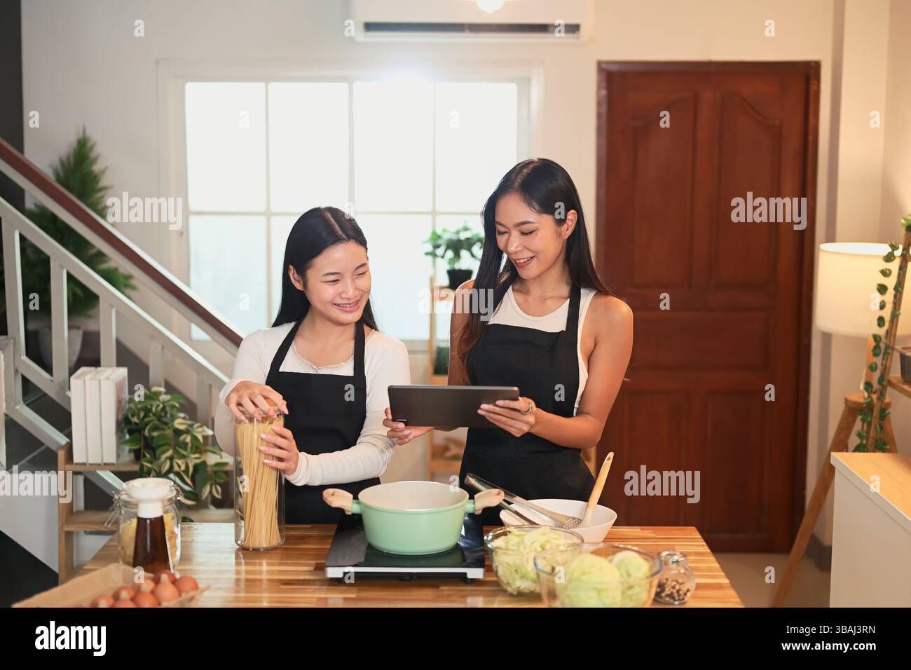 Asian mom and teenage daughter reading digital recipe together while ...