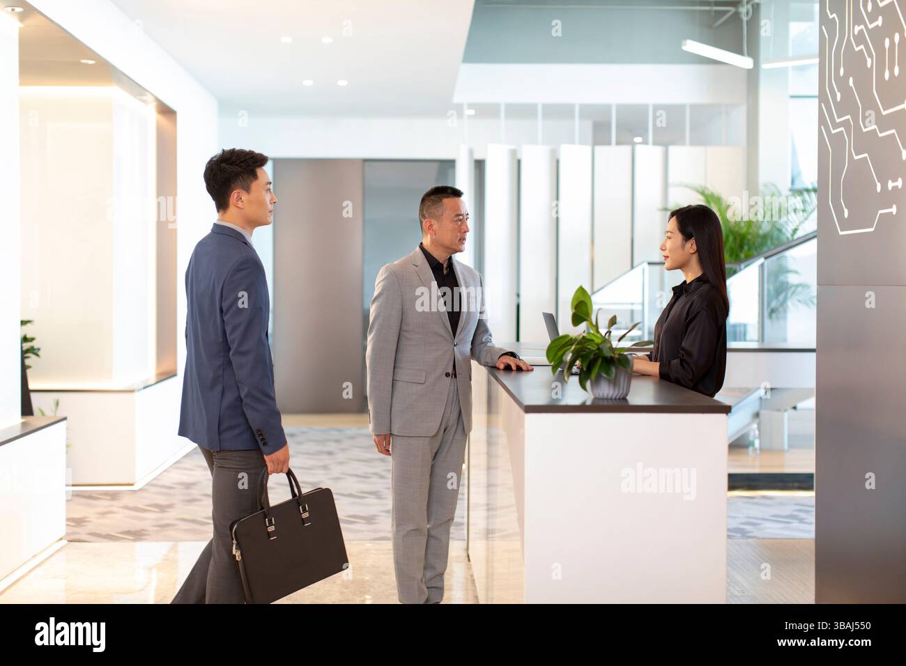 Chinese businessmen talking with female receptionist standing in office ...