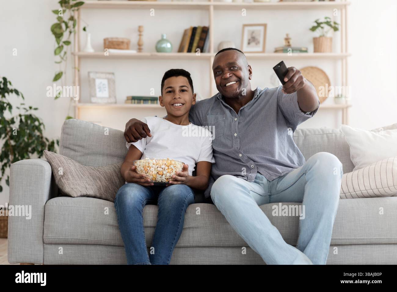 Middle-aged Black grandfather holding remote watching television with ...