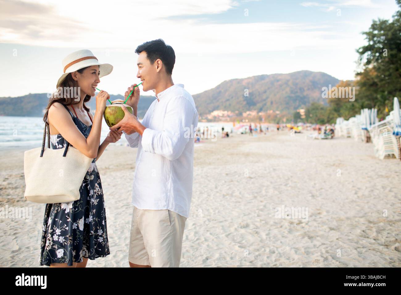 Smiling Chinese couple facing each other and drinking coconut water ...