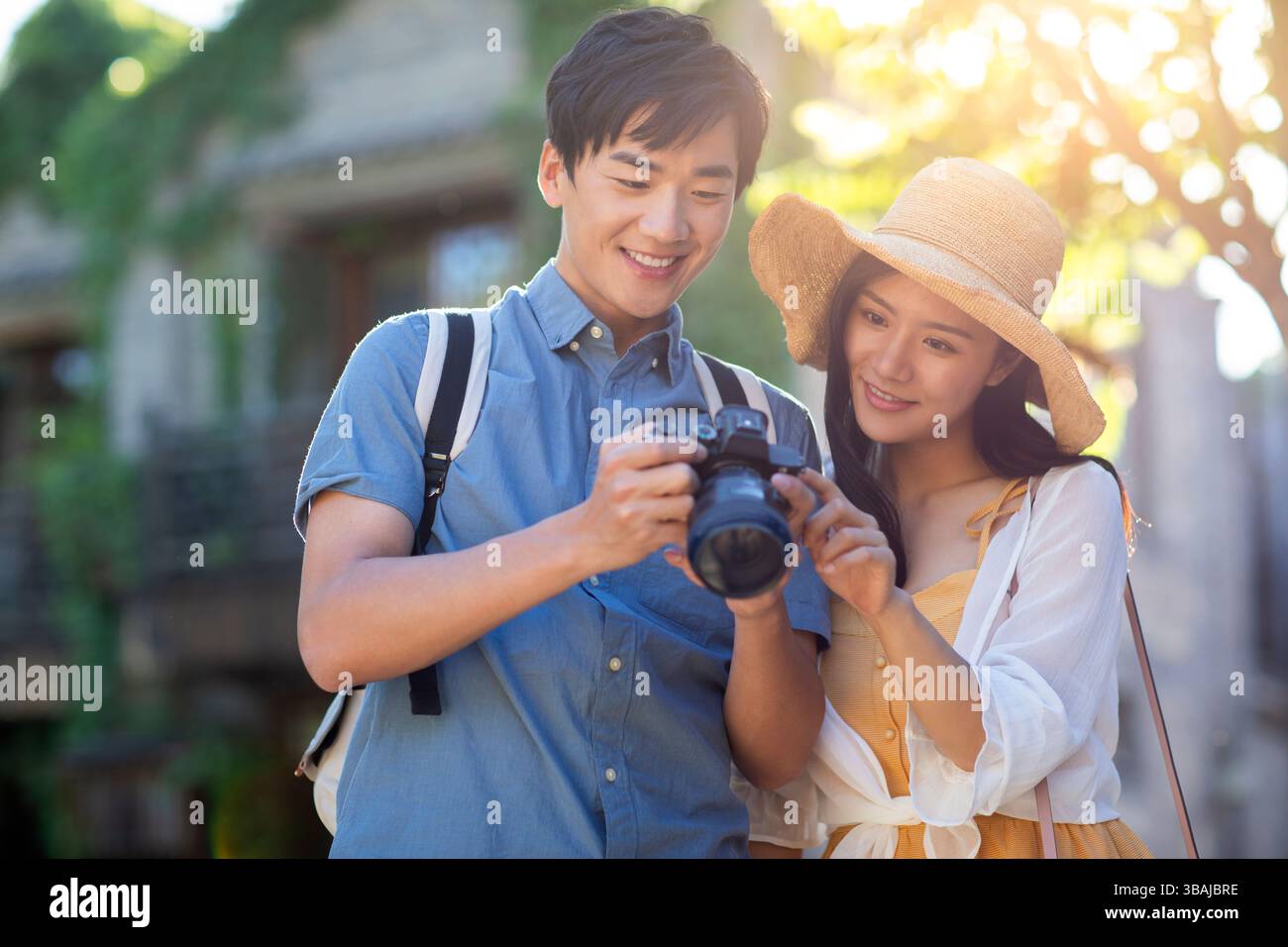 Smiling Chinese couple watching pictures on camera standing on street ...