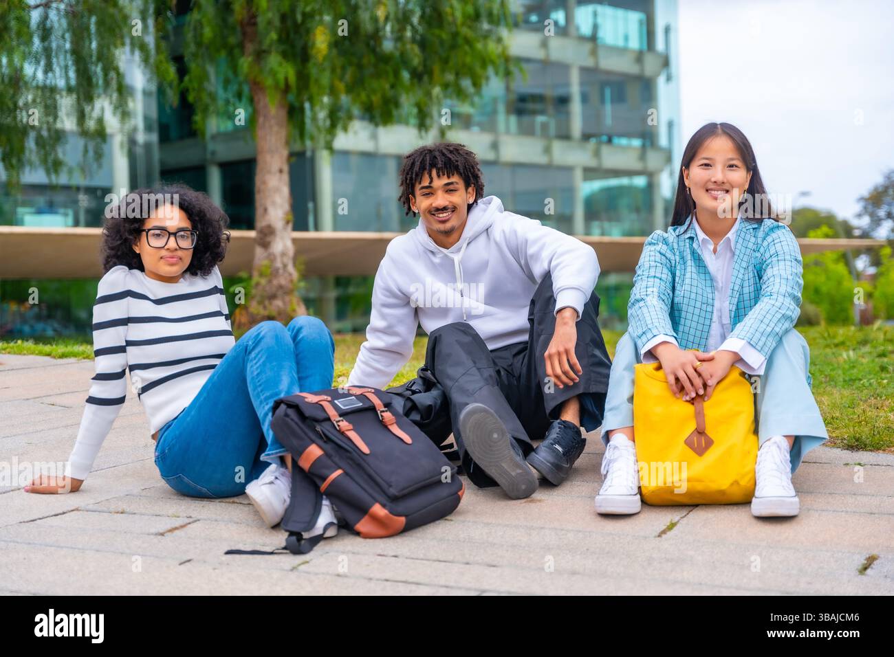 Portrait of three diverse cool university students sitting outside the ...
