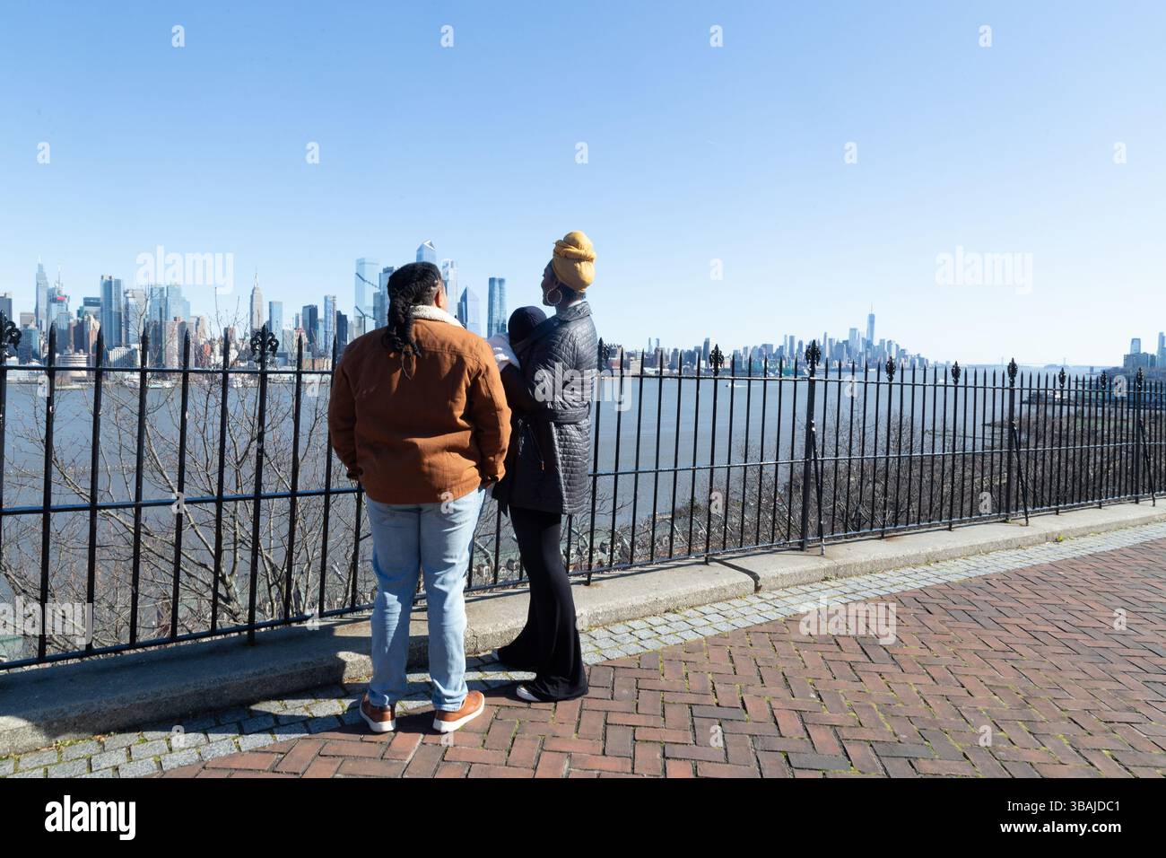 Black non-binary person standing with Black wife carrying their baby in ...