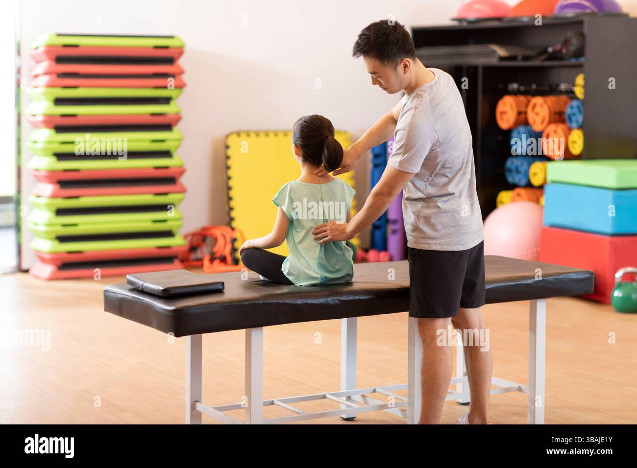 Chinese little girl having physiotherapy with male therapist in gym ...