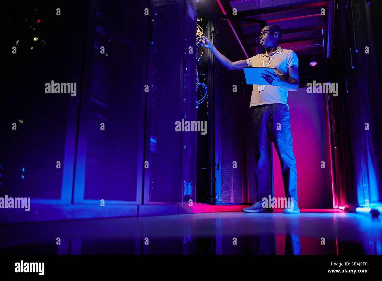 Full length portrait of African American system administrator setting up server network in data ...